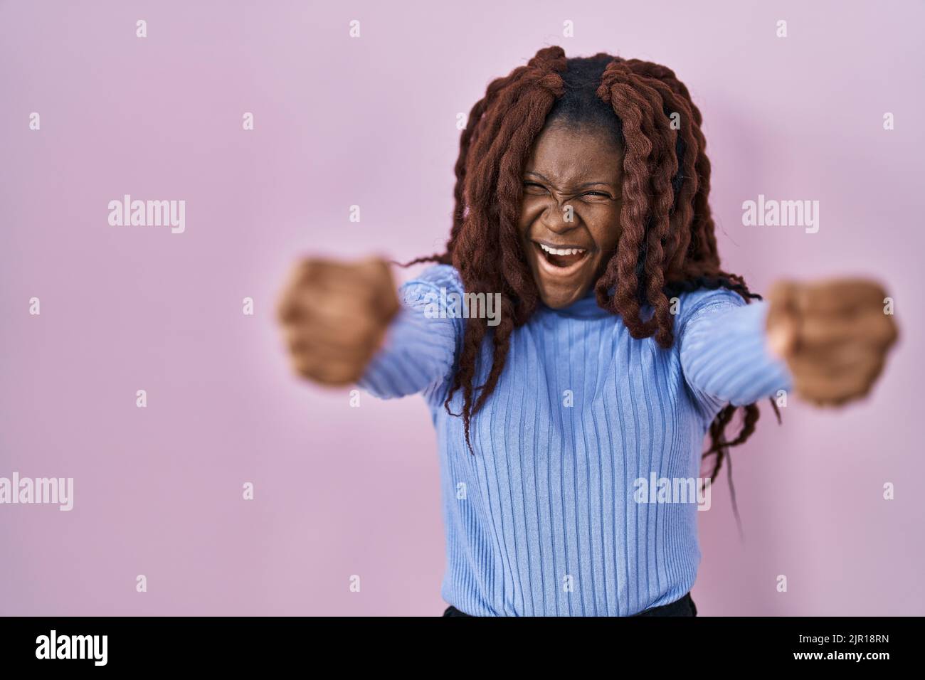 African woman standing over pink background angry and mad raising fists ...