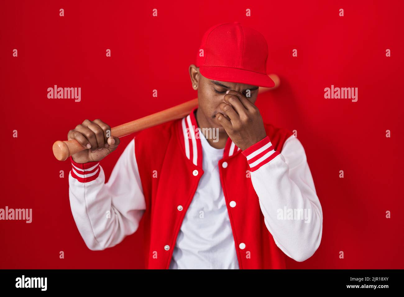 Young hispanic man playing baseball holding bat tired rubbing nose and ...