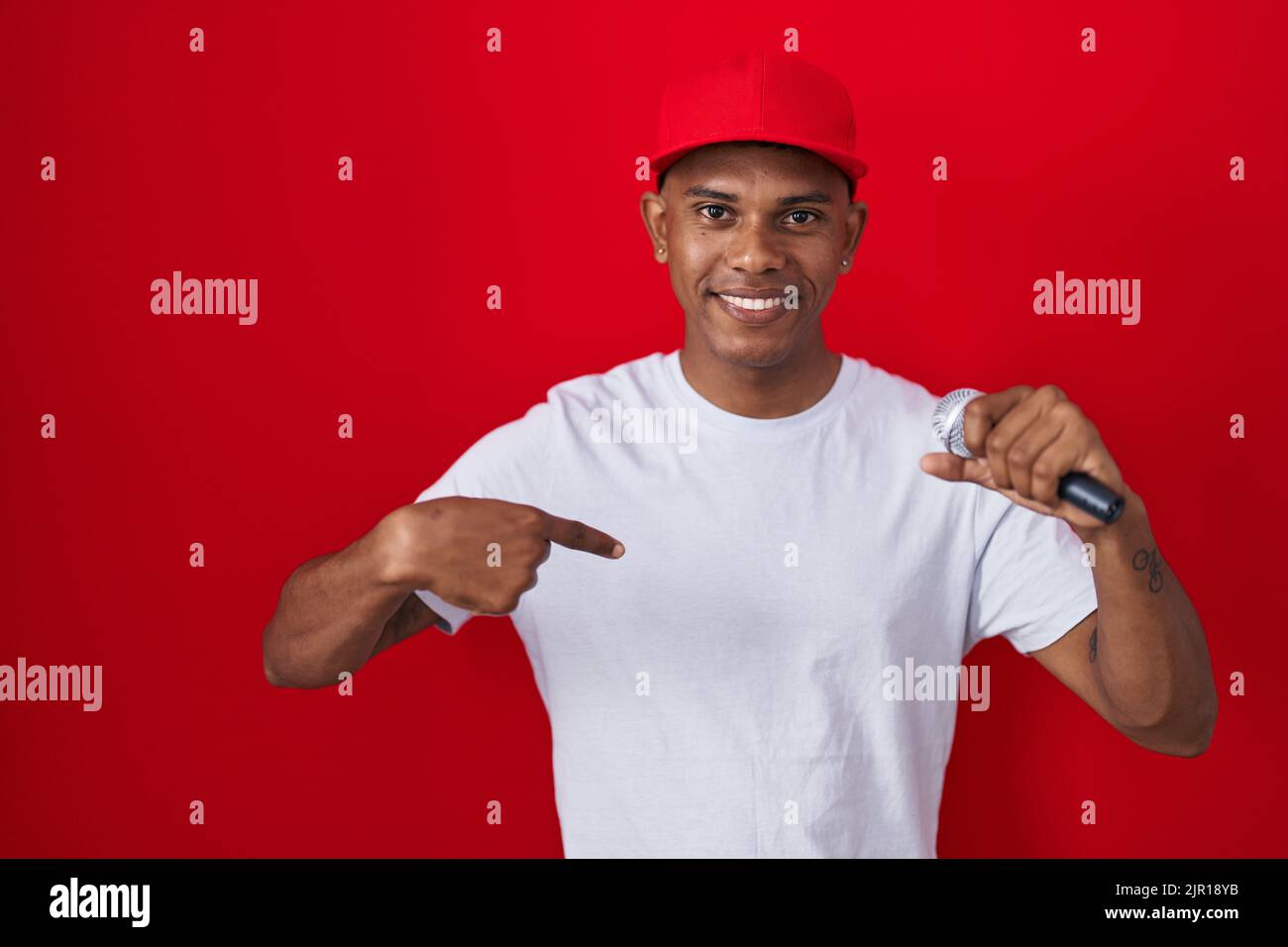 Young hispanic man singing song using microphone pointing finger to one ...