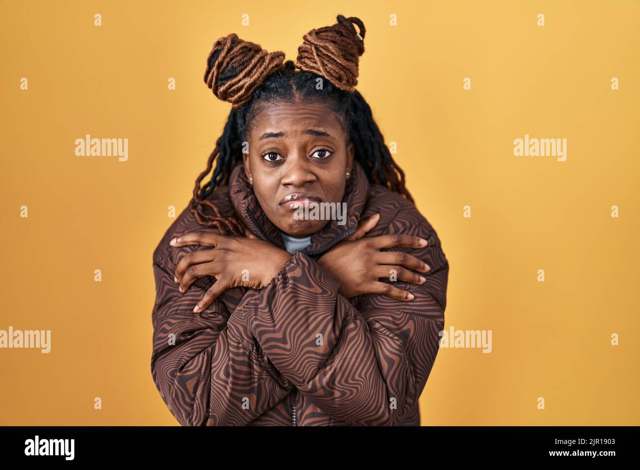 African woman with braided hair standing over yellow background shaking ...