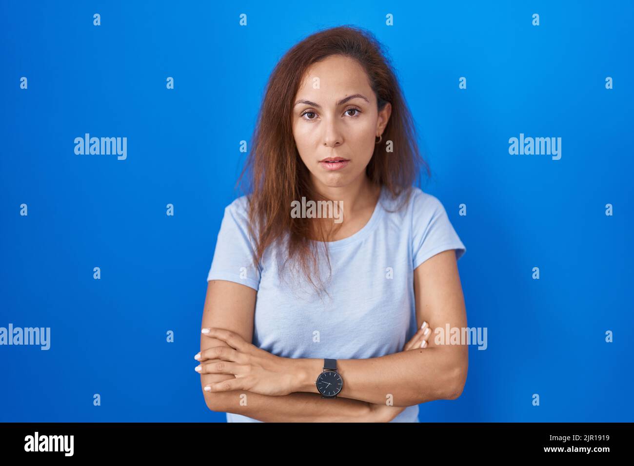 Brunette woman standing over blue background looking sleepy and tired ...