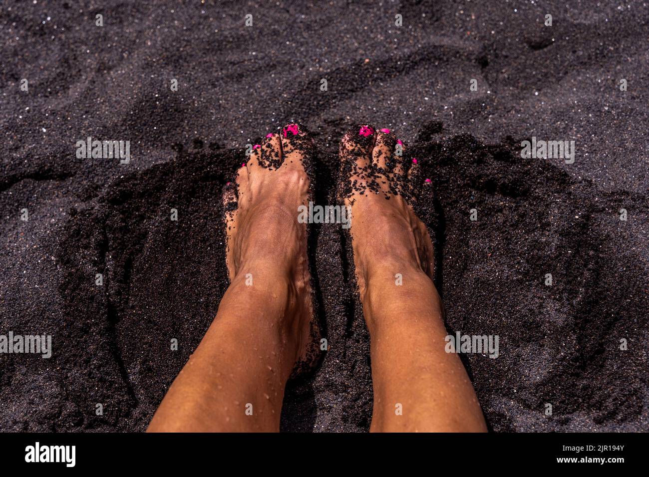 closeup of feet of woman lying down on a black volcanic tropical beach ...