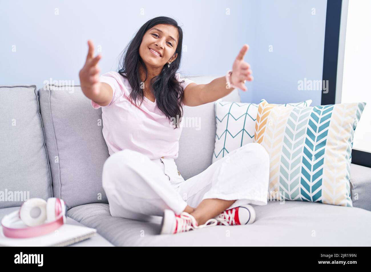 Young hispanic woman sitting on the sofa at home looking at the camera ...
