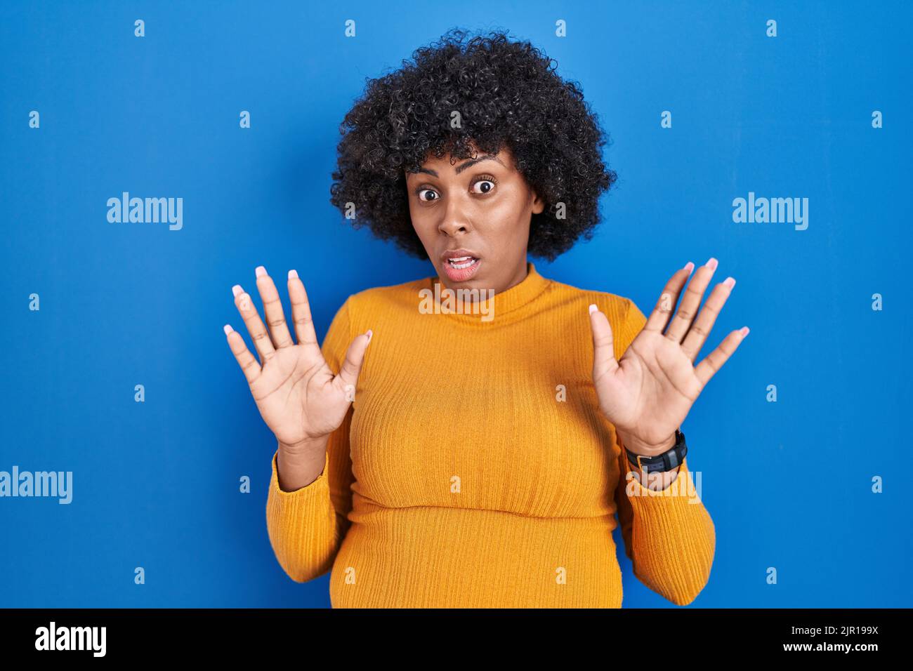 Black woman with curly hair standing over blue background moving away ...