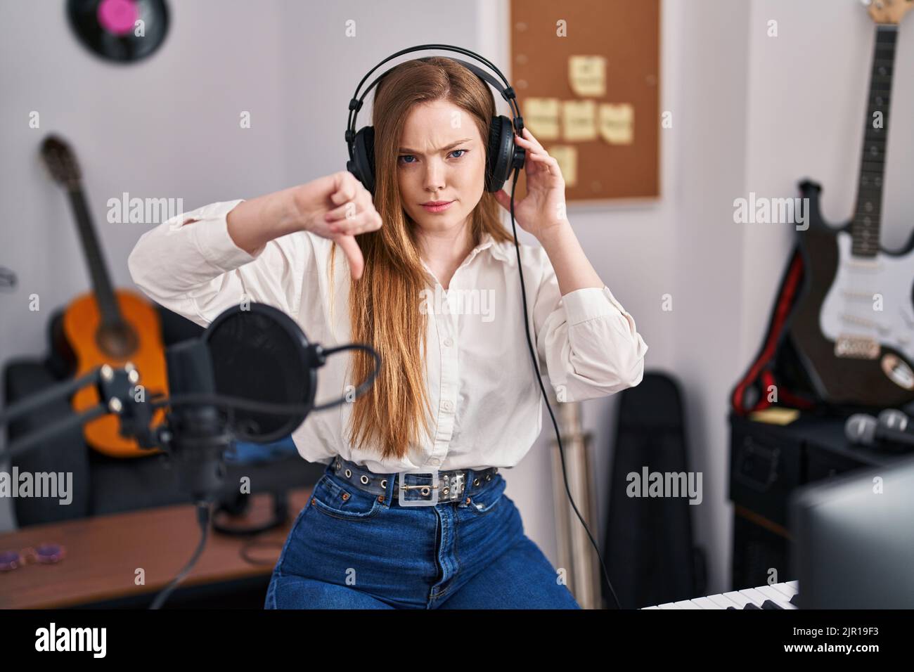 Young caucasian woman recording song at music studio with angry face ...