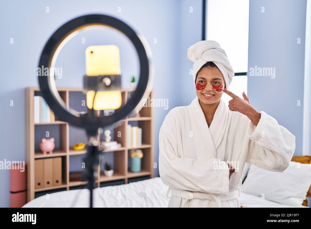 Hispanic woman with dark hair recording beauty tutorial with smartphone ...