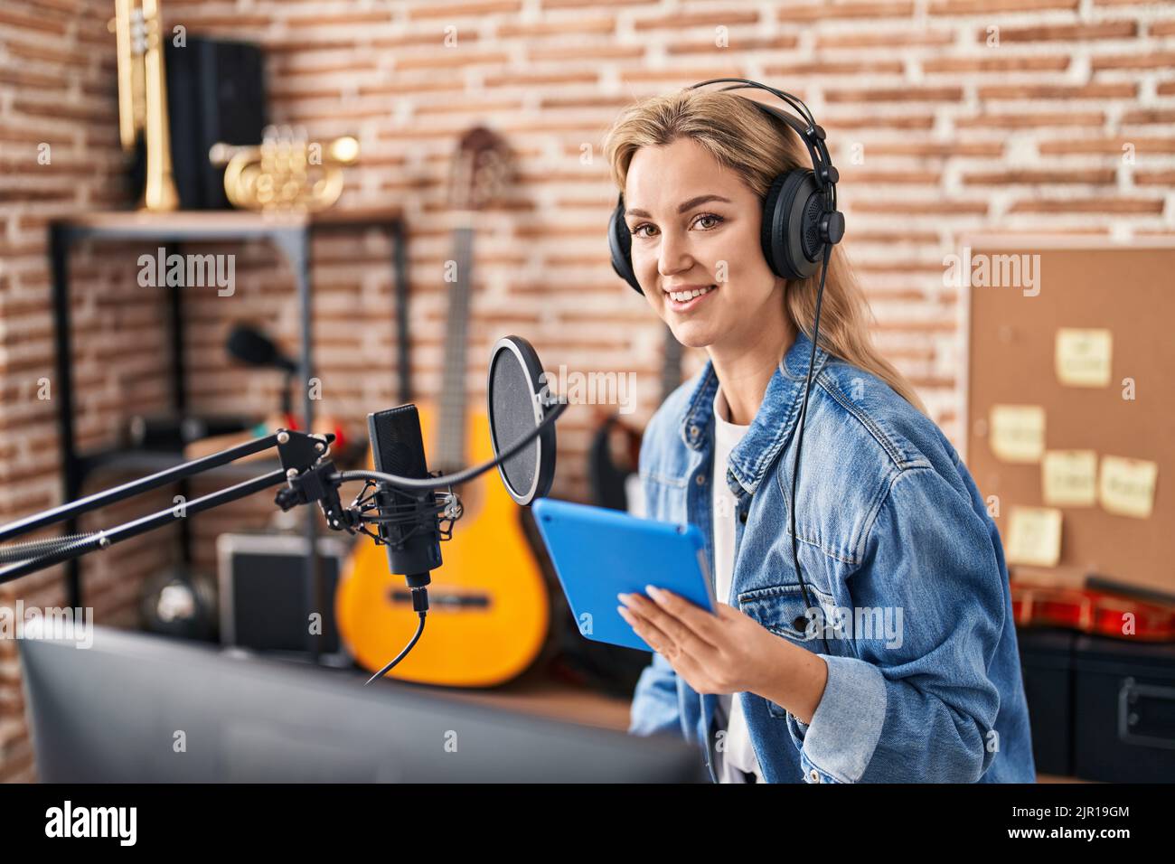Young blonde woman artist singing song using touchpad at music studio ...