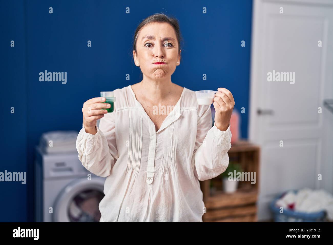 Middle age hispanic woman holding laundry detergent and laundry powder ...