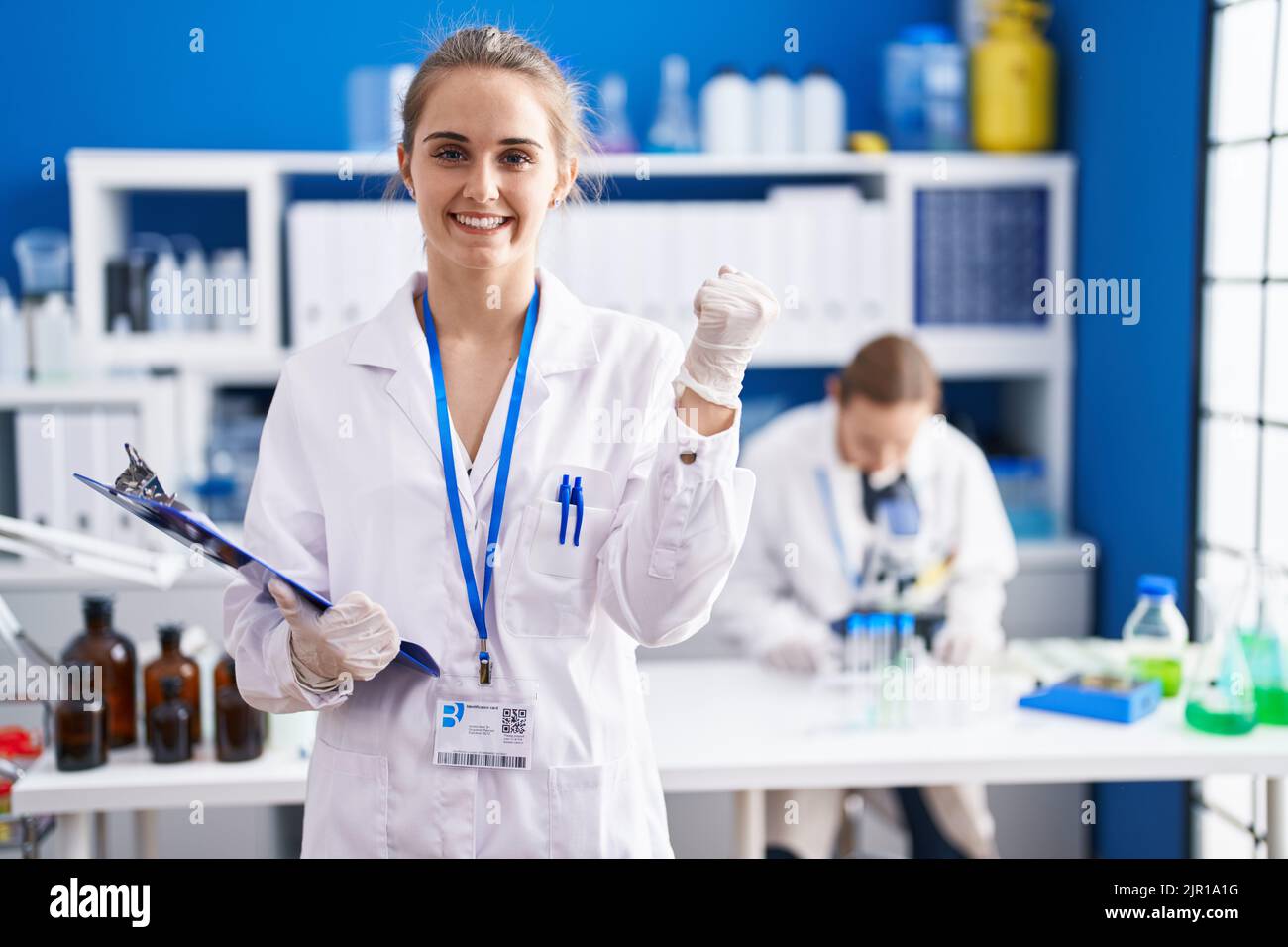 Blonde woman working at scientist laboratory screaming proud ...