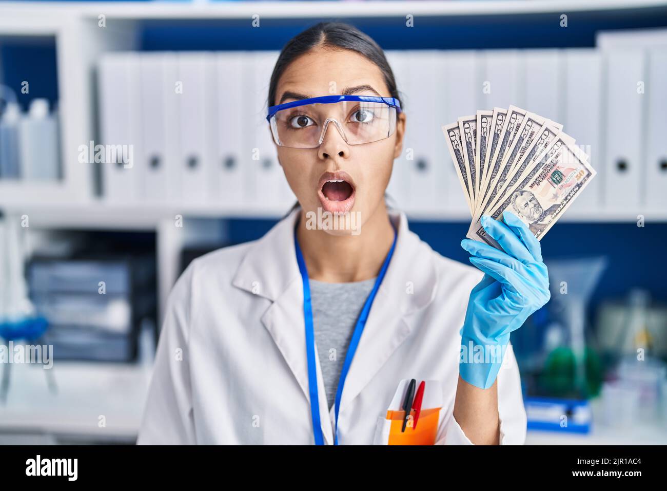 Young brazilian woman working at scientist laboratory holding money ...
