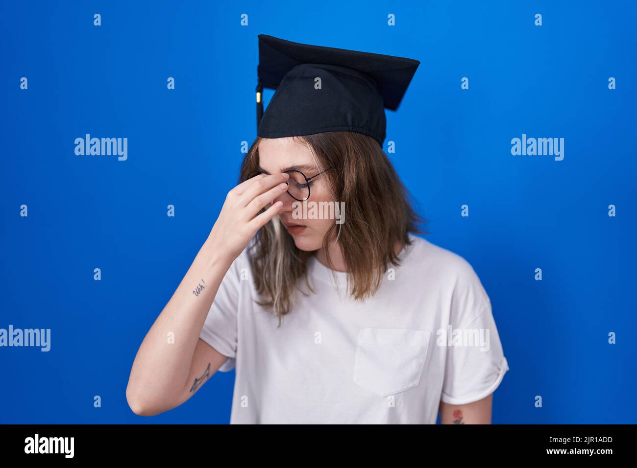 Blonde caucasian woman wearing graduation cap tired rubbing nose and ...