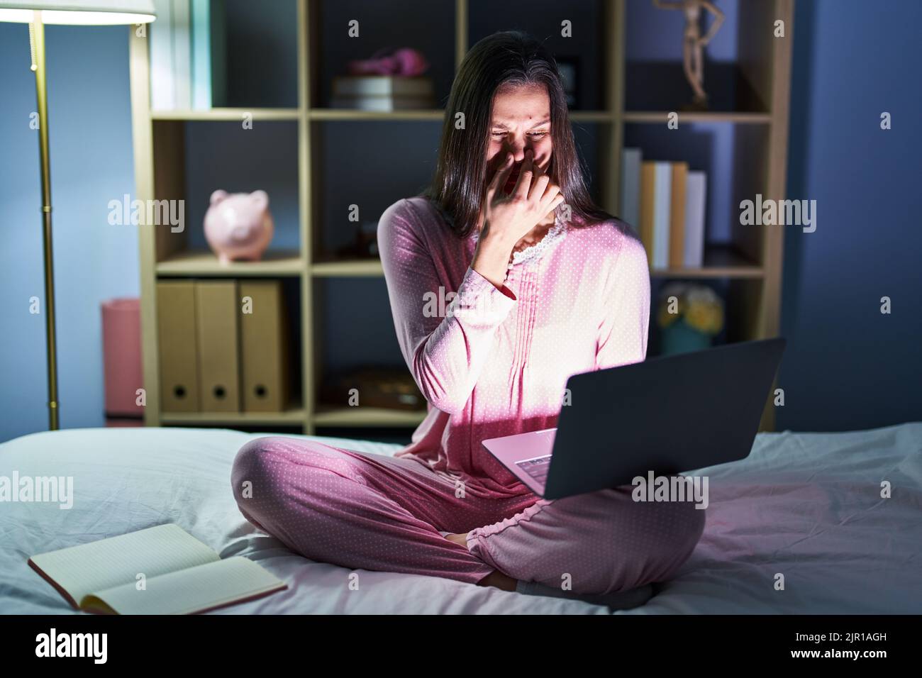 Young hispanic woman using computer laptop on the bed smelling ...