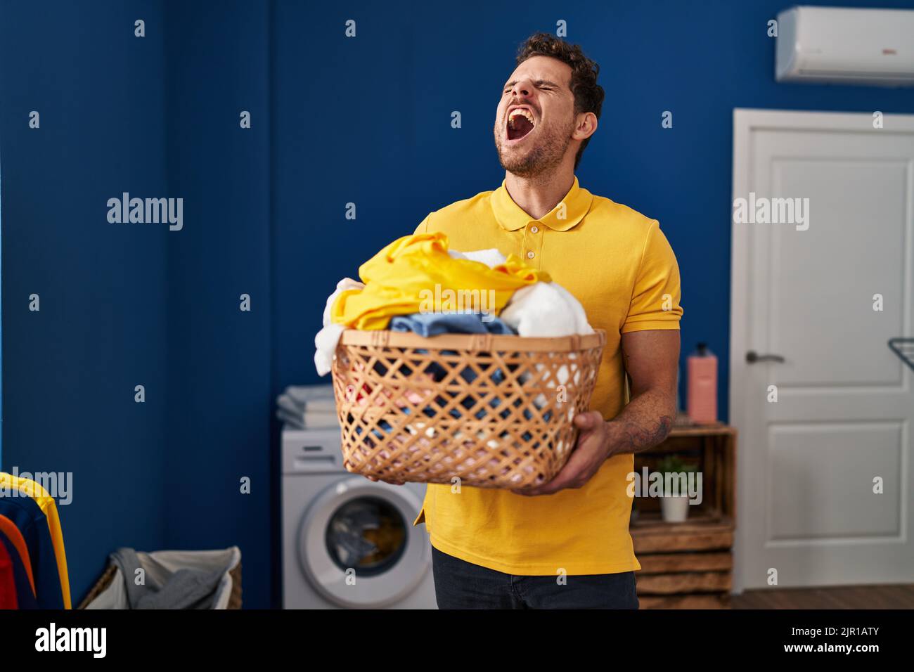 Young hispanic man holding laundry basket angry and mad screaming ...