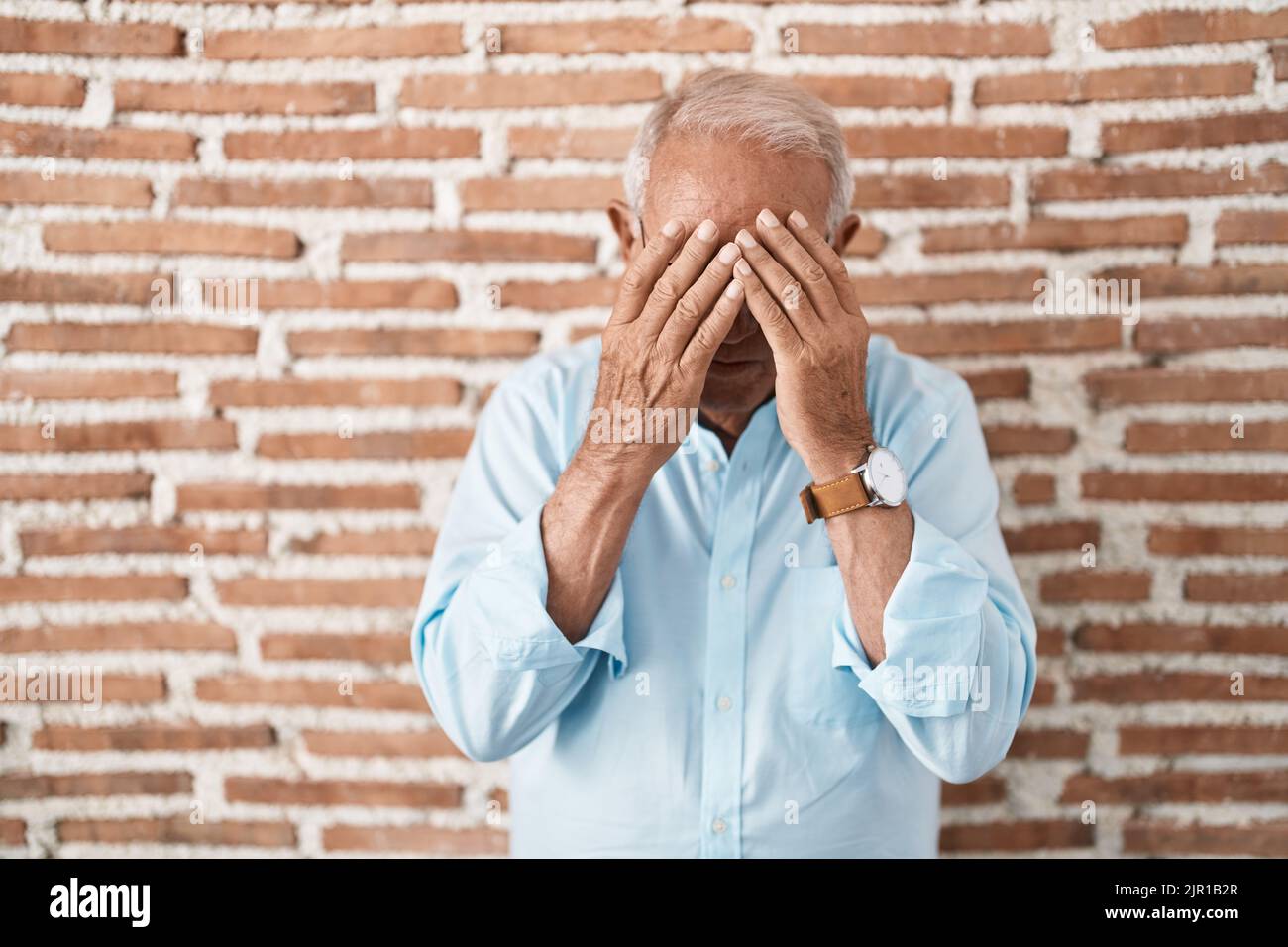 Senior man with grey hair standing over bricks wall with sad expression ...