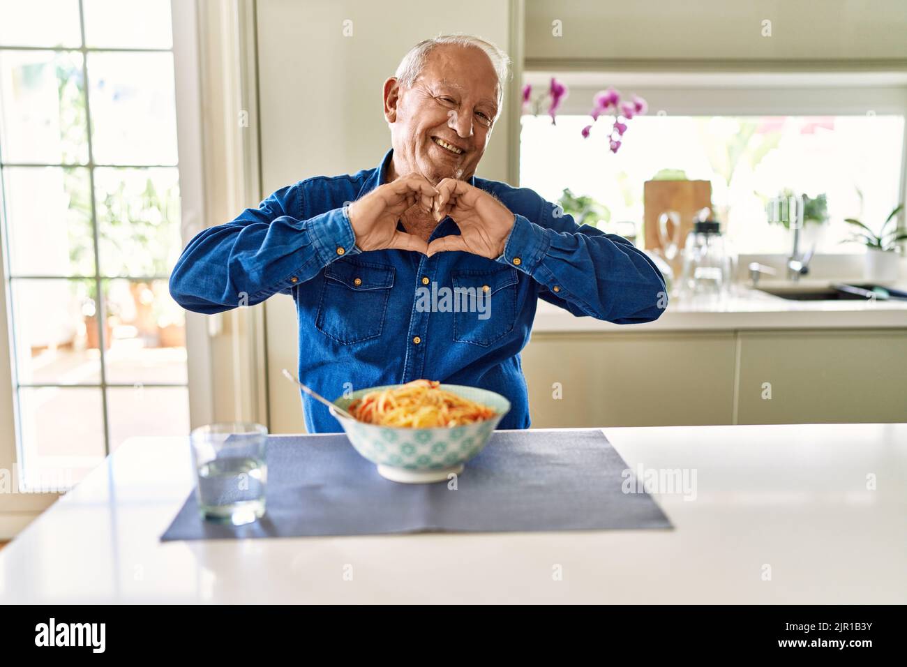 Senior man with grey hair eating pasta spaghetti at home smiling in ...