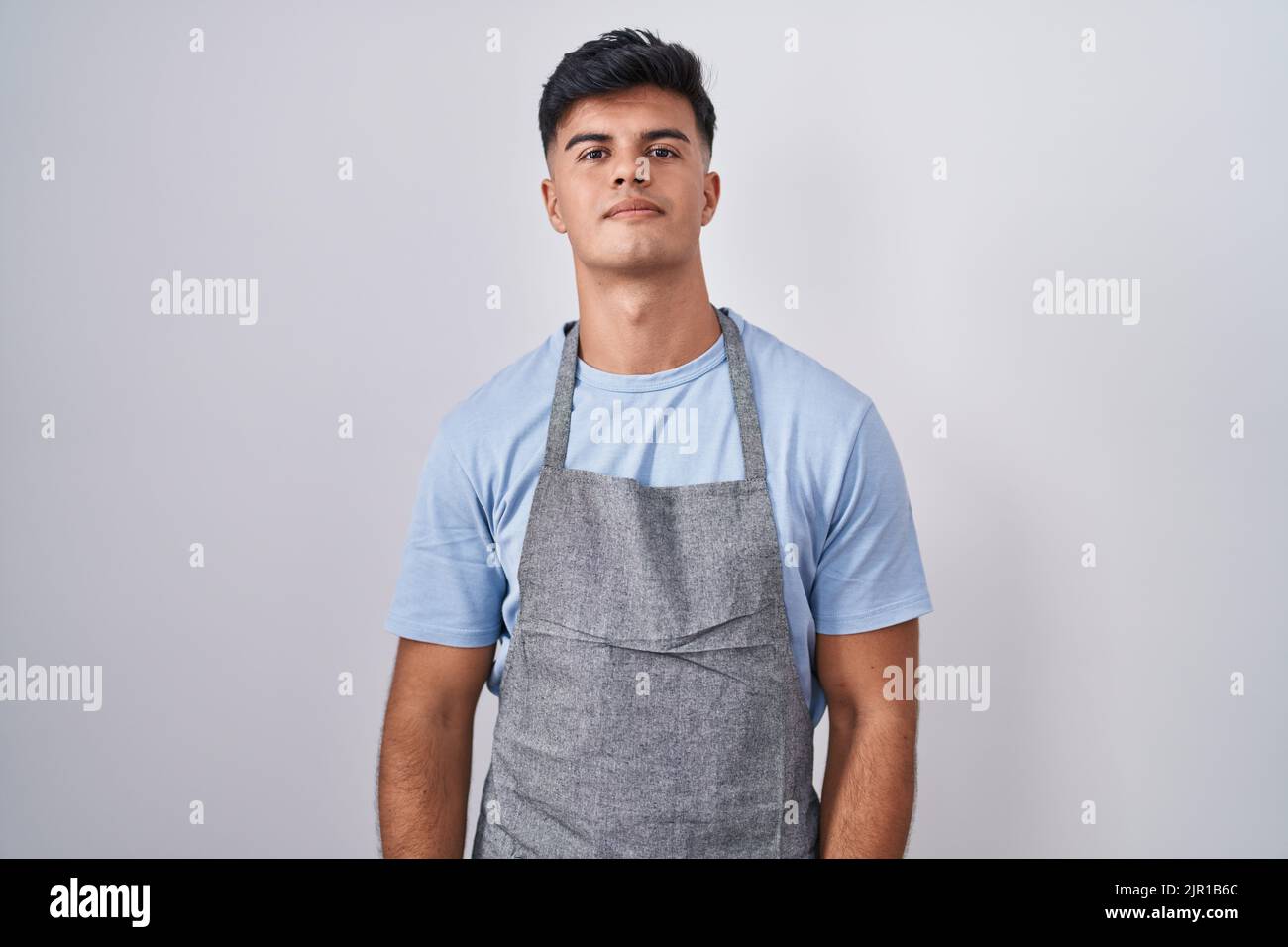 Hispanic young man wearing apron over white background relaxed with ...
