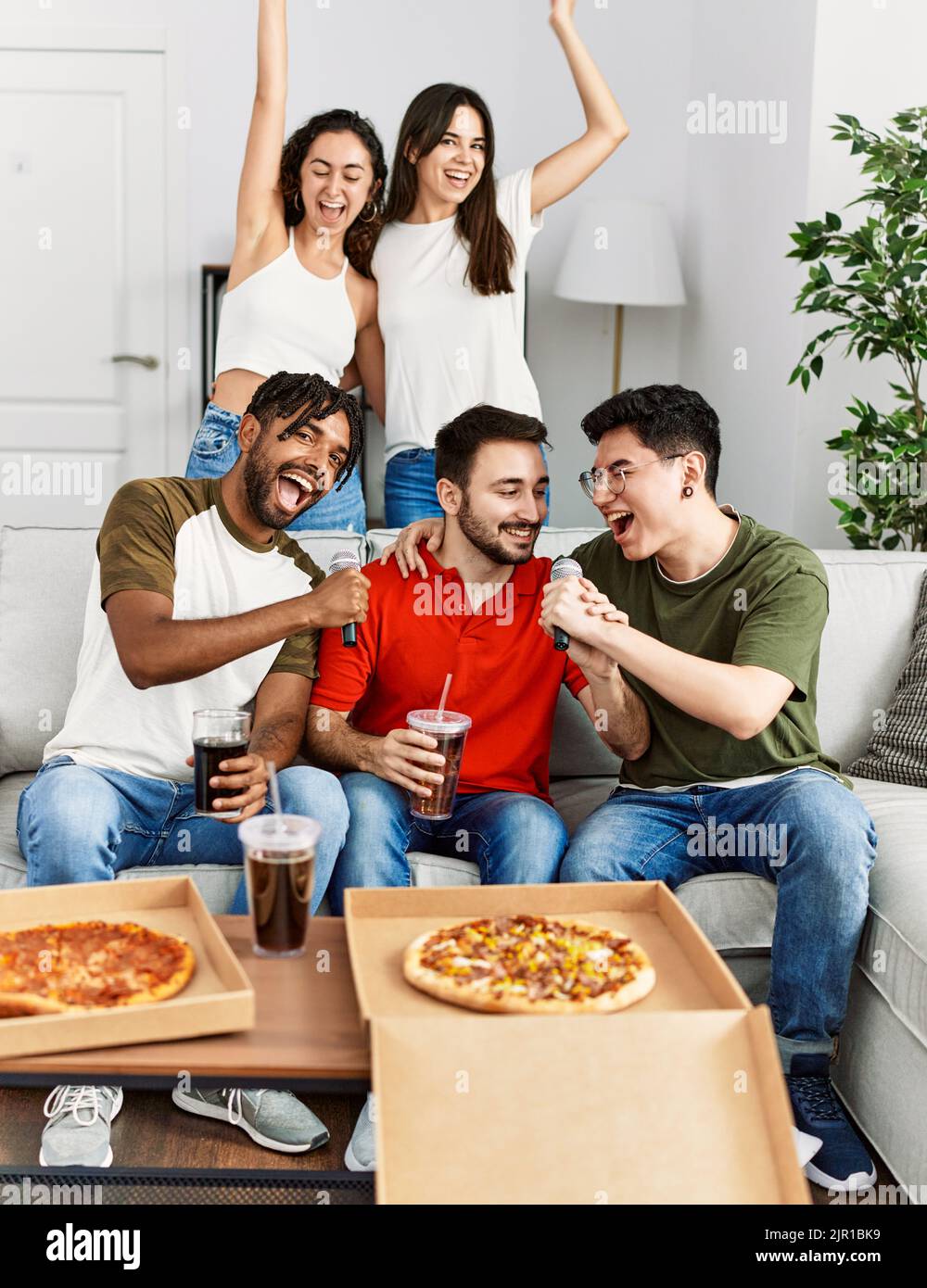 Group of young friends having party eating italian pizza and singing ...