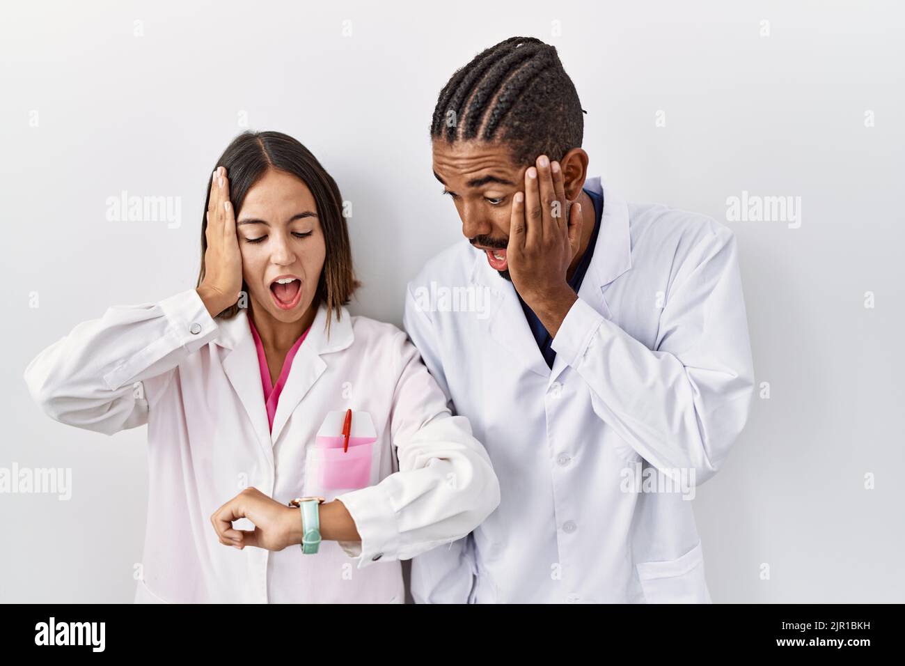 Young hispanic doctors standing over white background looking at the ...