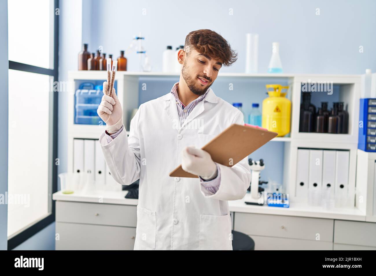 Young arab man scientist holding test tube and clipboard at laboratory ...