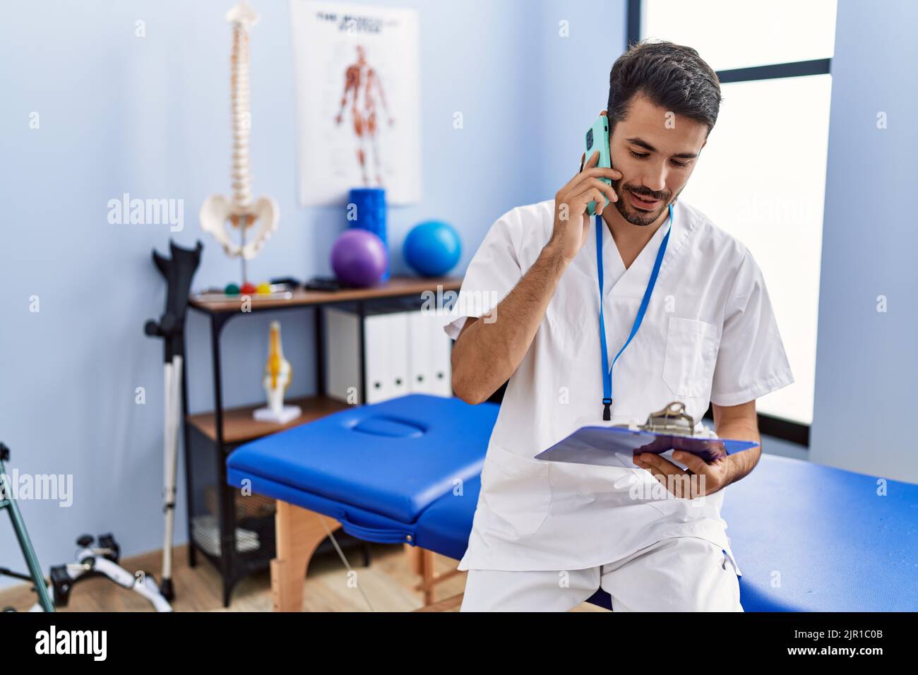 Young hispanic man wearing physiotherapist uniform talking on the ...