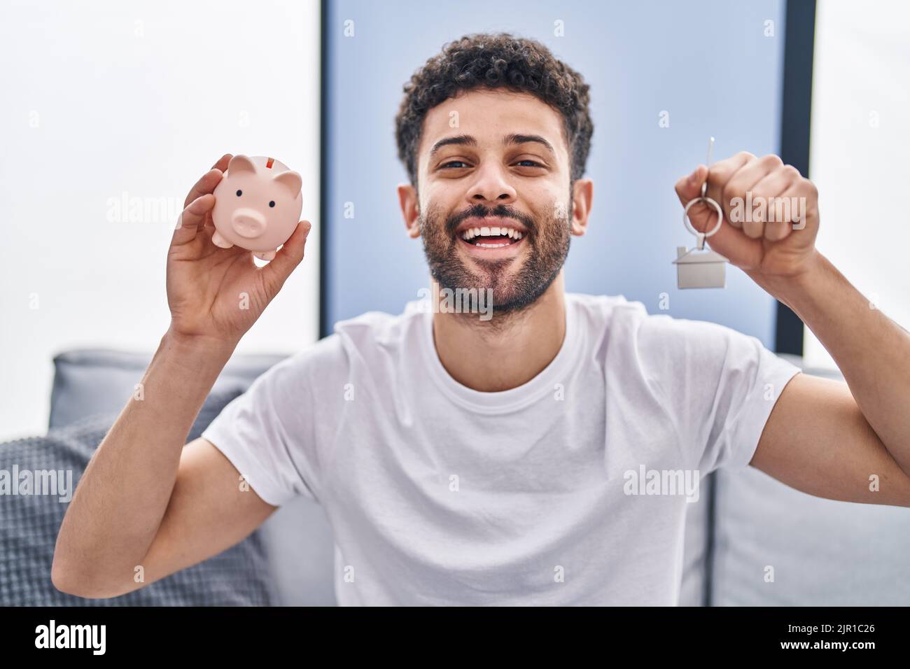 Arab man holding piggy bank and house keys smiling and laughing hard ...