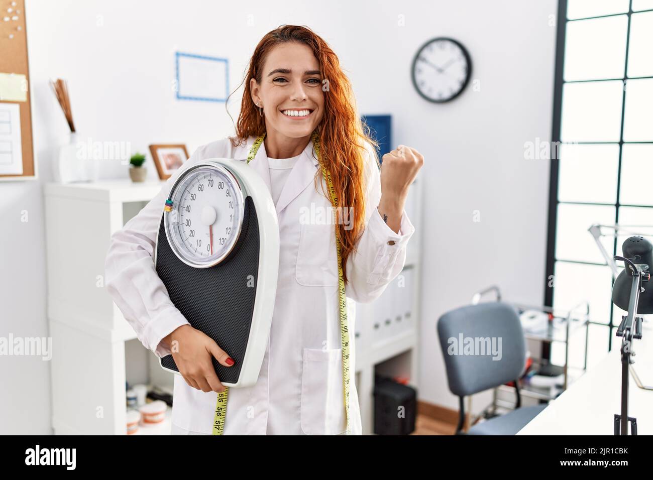 Young redhead woman nutritionist doctor holding weighing machine ...