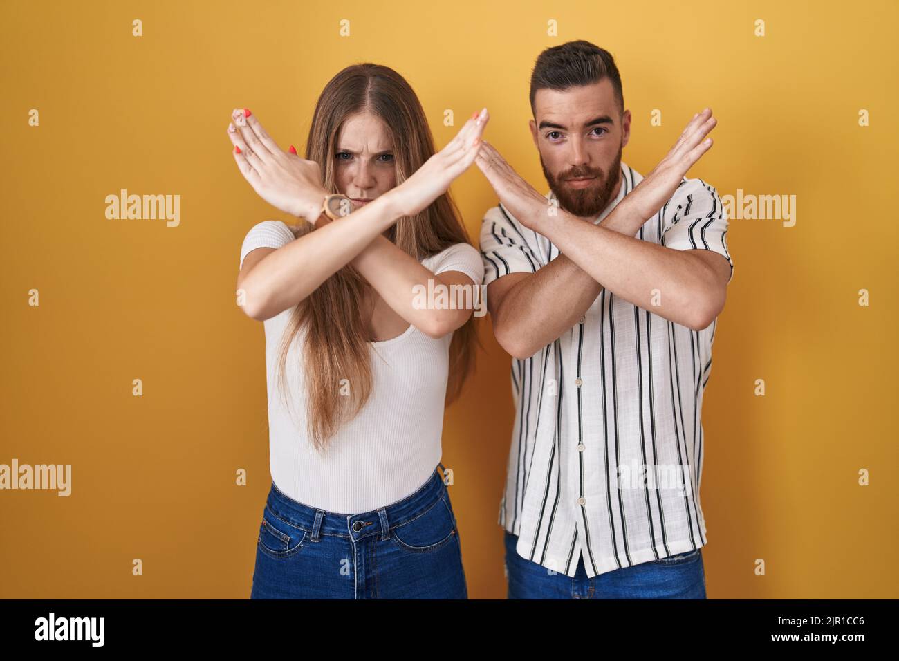 Young couple standing over yellow background rejection expression ...