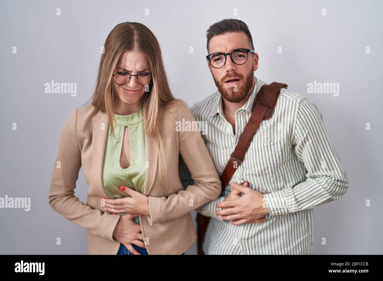 Young couple standing over white background with hand on stomach ...