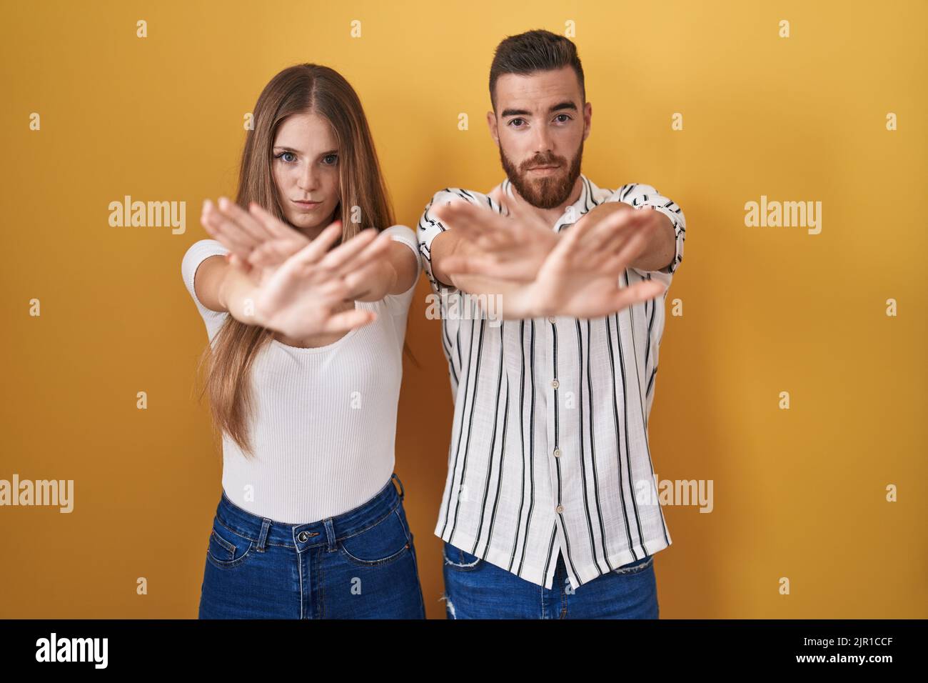 Young couple standing over yellow background rejection expression ...