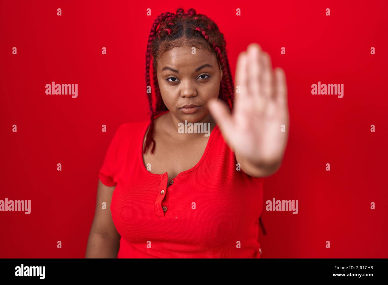 African american woman with braided hair standing over red background ...