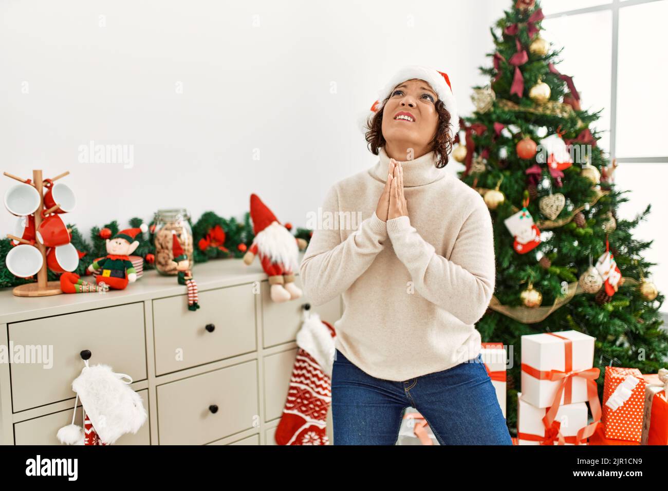 Middle age hispanic woman standing by christmas tree begging and ...