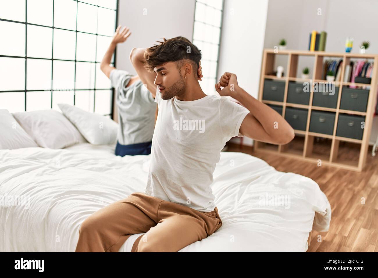 Two hispanic men couple waking up stretching arms and yawning at ...