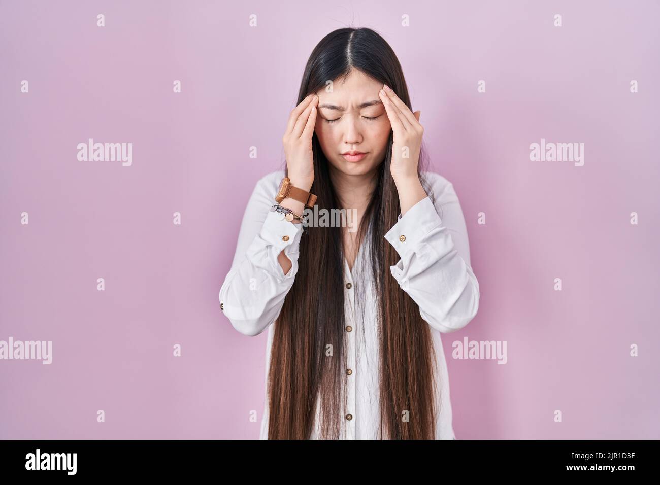 Chinese young woman standing over pink background with hand on head ...