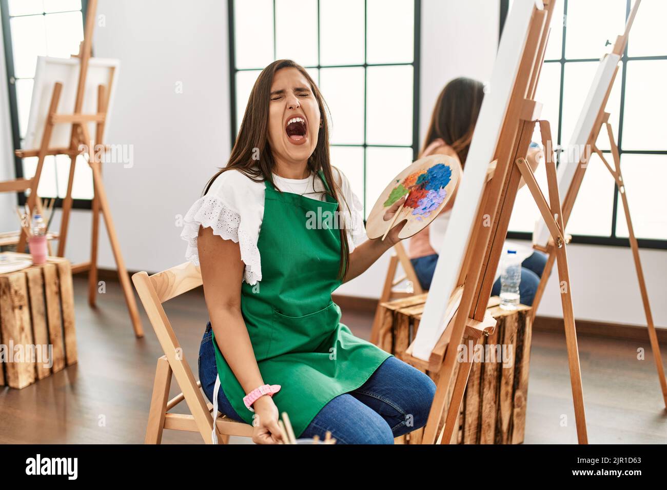 Young hispanic artist women painting on canvas at art studio angry and ...