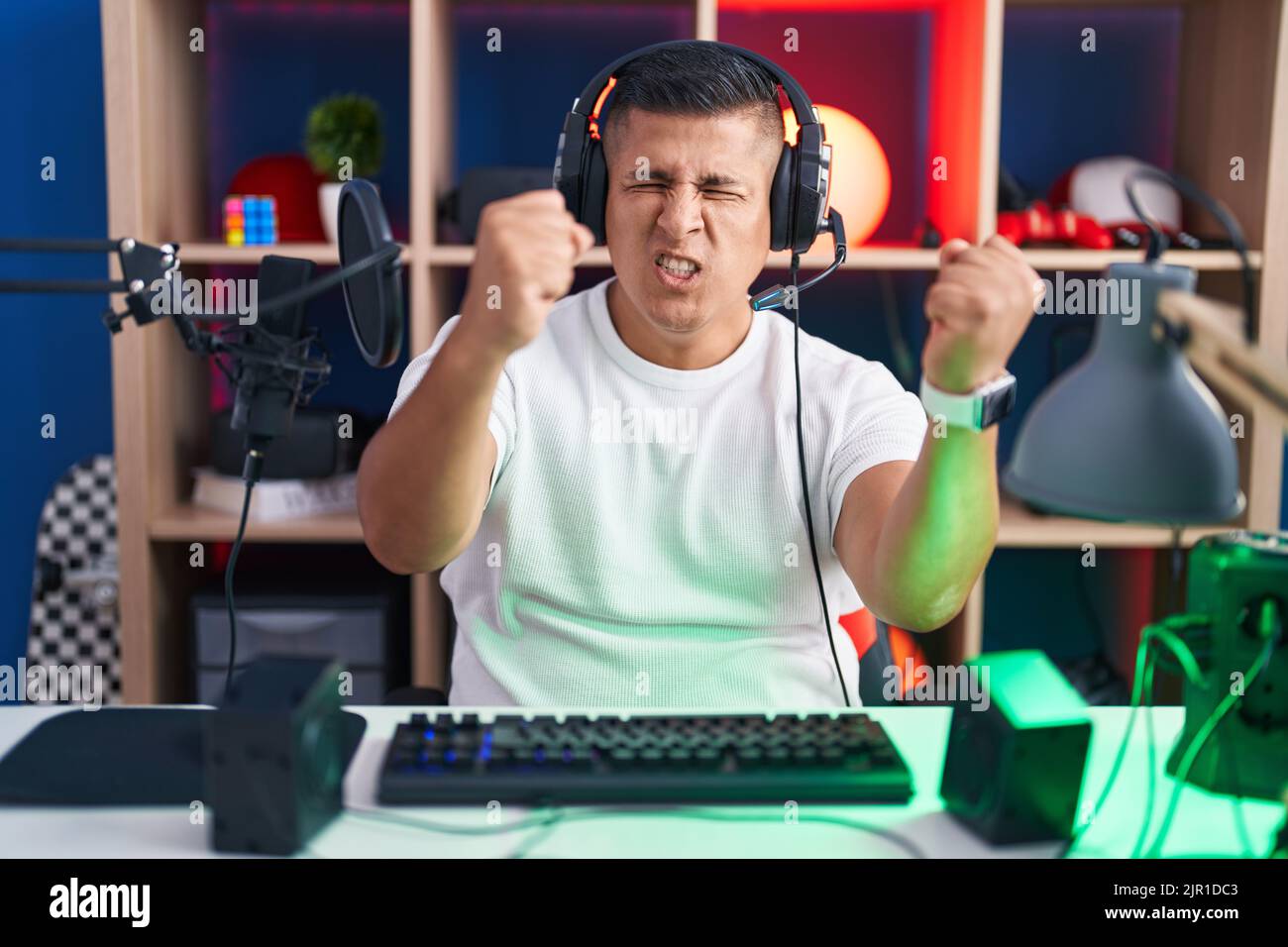Young hispanic man playing video games angry and mad raising fists ...