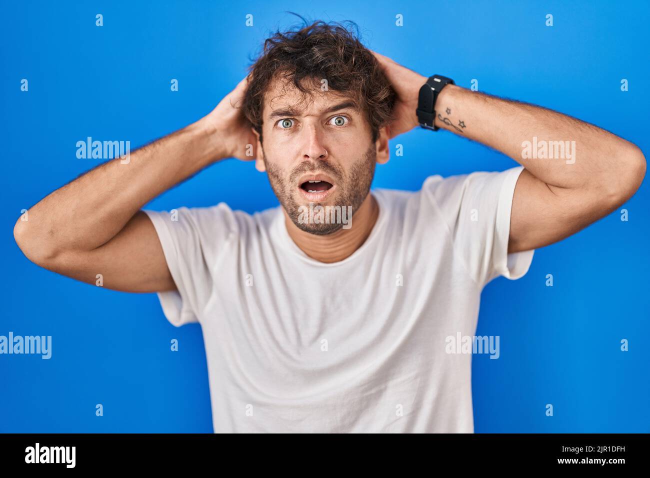 Hispanic young man standing over blue background crazy and scared with ...