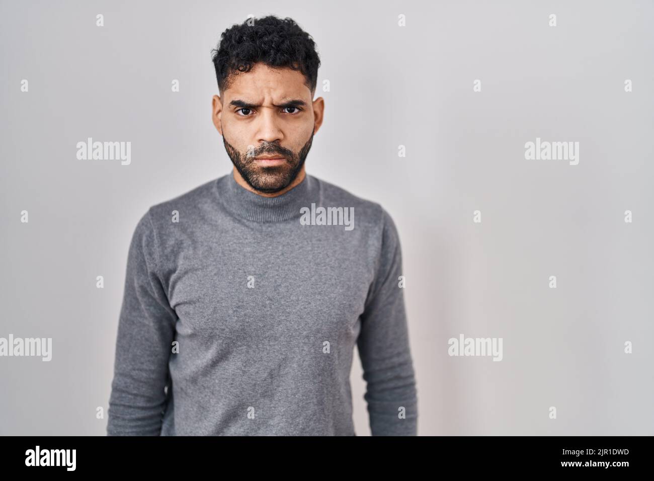 Hispanic man with beard standing over white background skeptic and ...