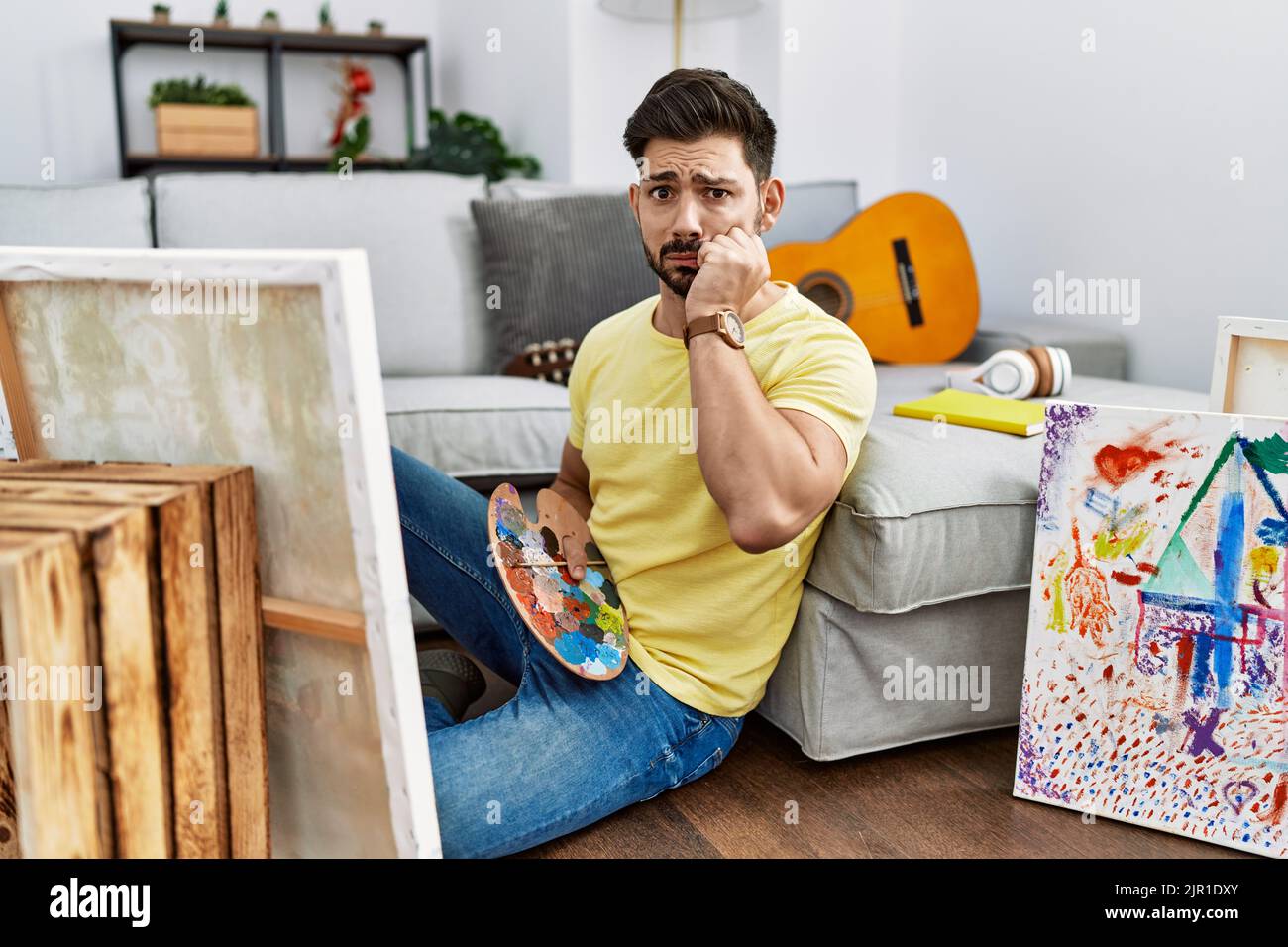 Young man with beard painting canvas at home looking stressed and ...