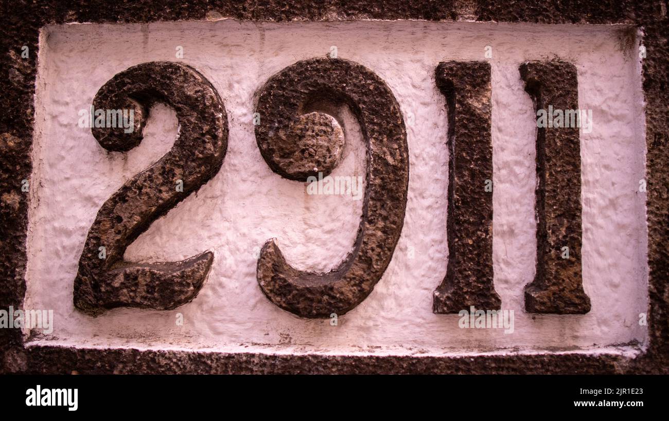 The numbers 2911 in grey cement, with a white painted background ...
