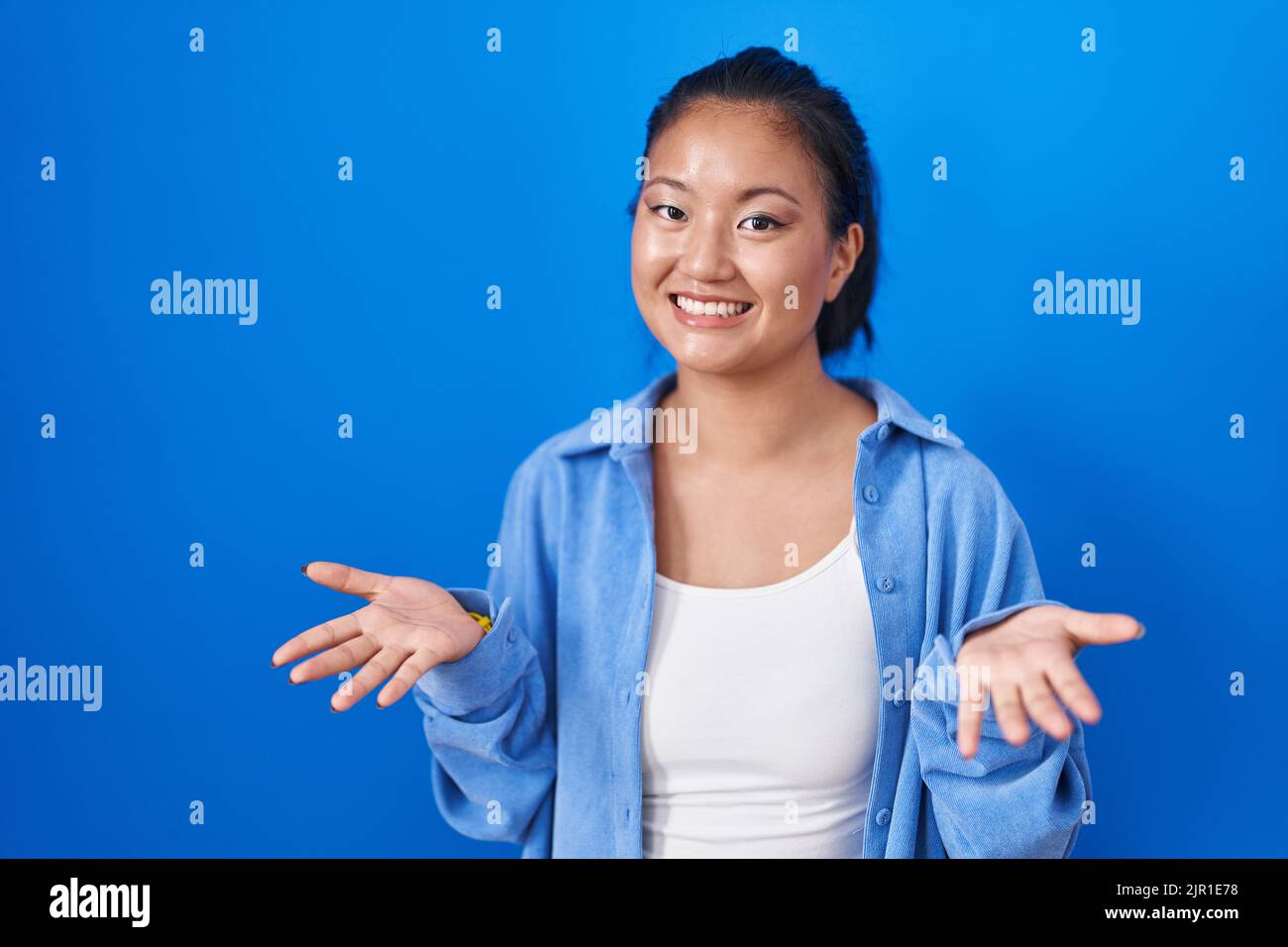 Asian young woman standing over blue background smiling cheerful ...