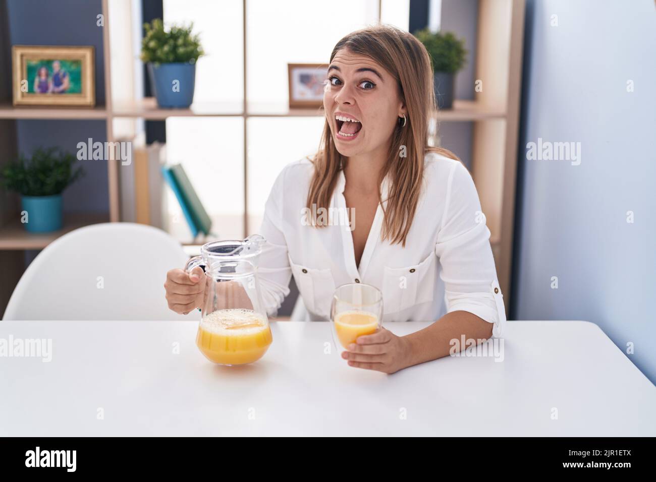 Young hispanic woman drinking glass of orange juice celebrating crazy ...
