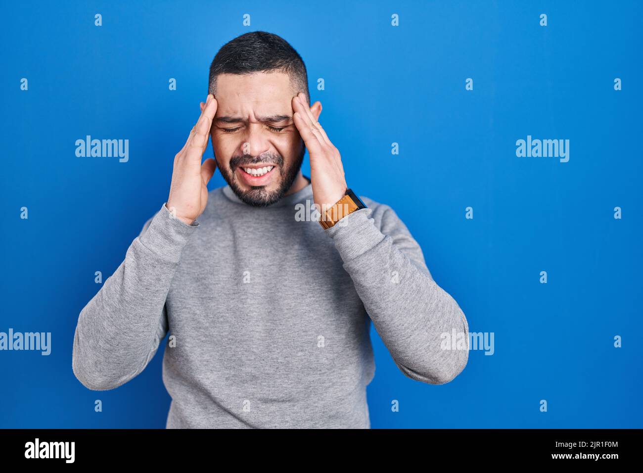Hispanic man standing over blue background with hand on head, headache ...
