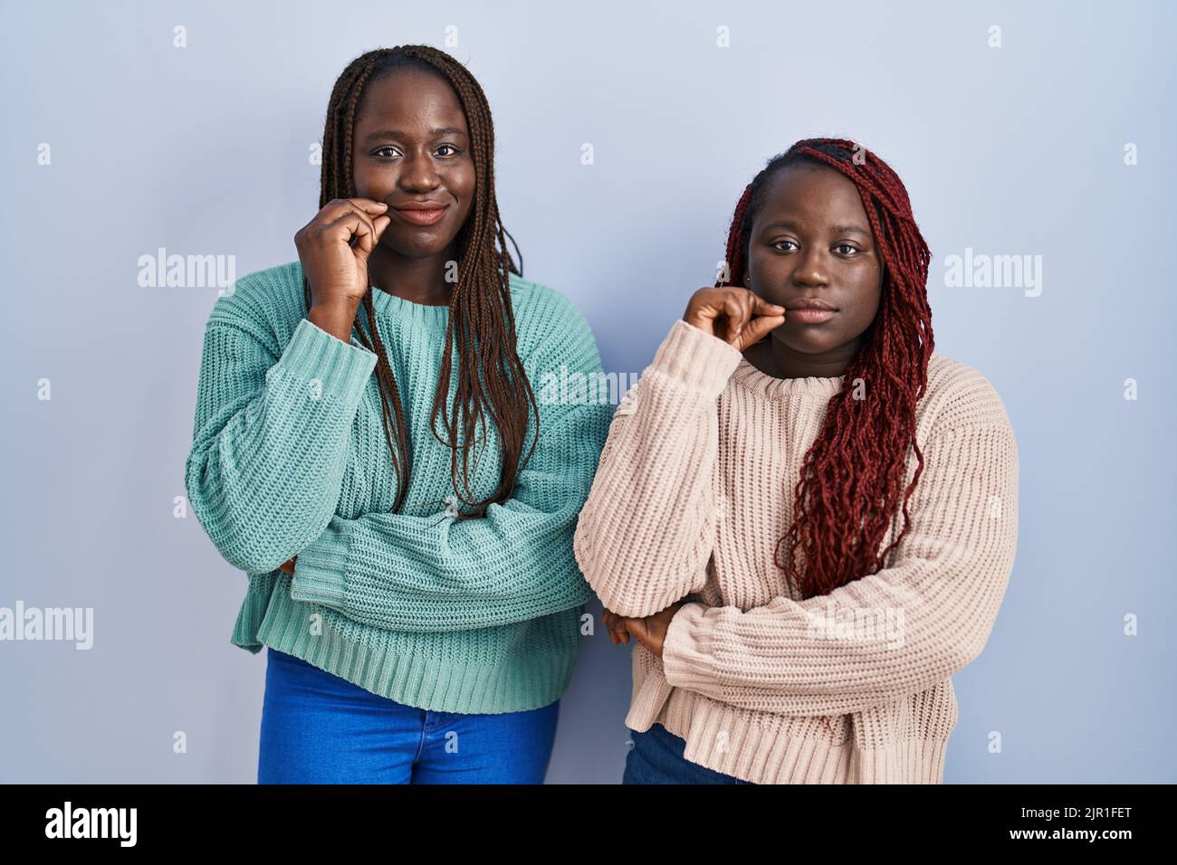 Two african woman standing over blue background mouth and lips shut as ...