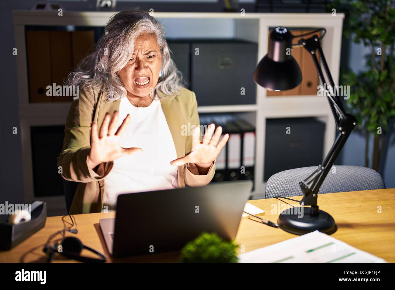 Middle age woman with grey hair working using computer laptop late at ...