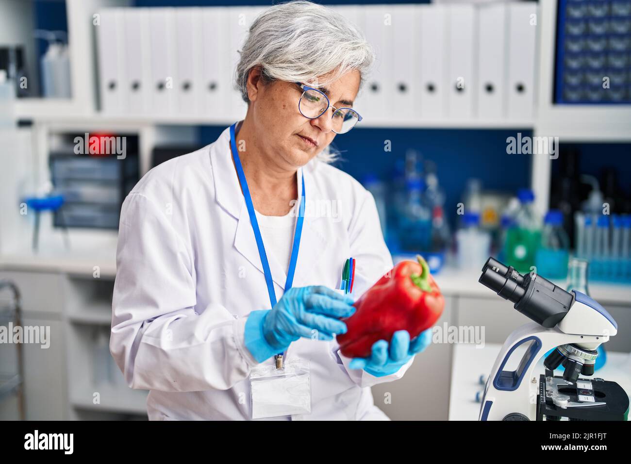 Middle age woman wearing scientist uniform analysing pepper at ...