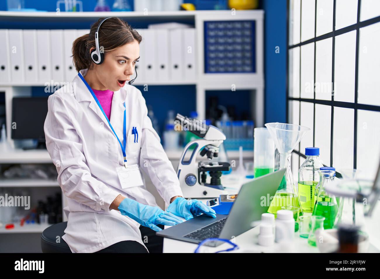 Hispanic woman working at scientist laboratory scared and amazed with ...