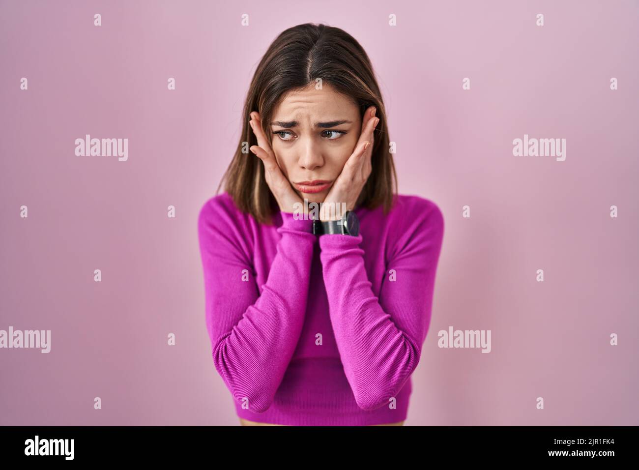 Hispanic woman standing over pink background tired hands covering face ...