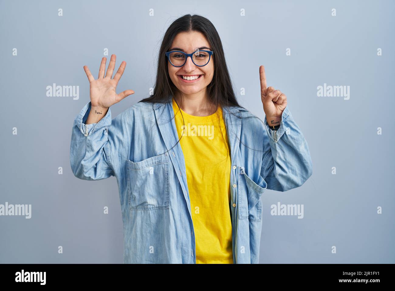 Young hispanic woman standing over blue background showing and pointing ...