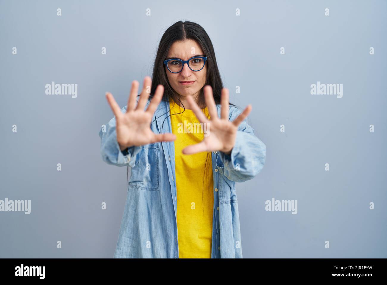 Young hispanic woman standing over blue background afraid and terrified ...