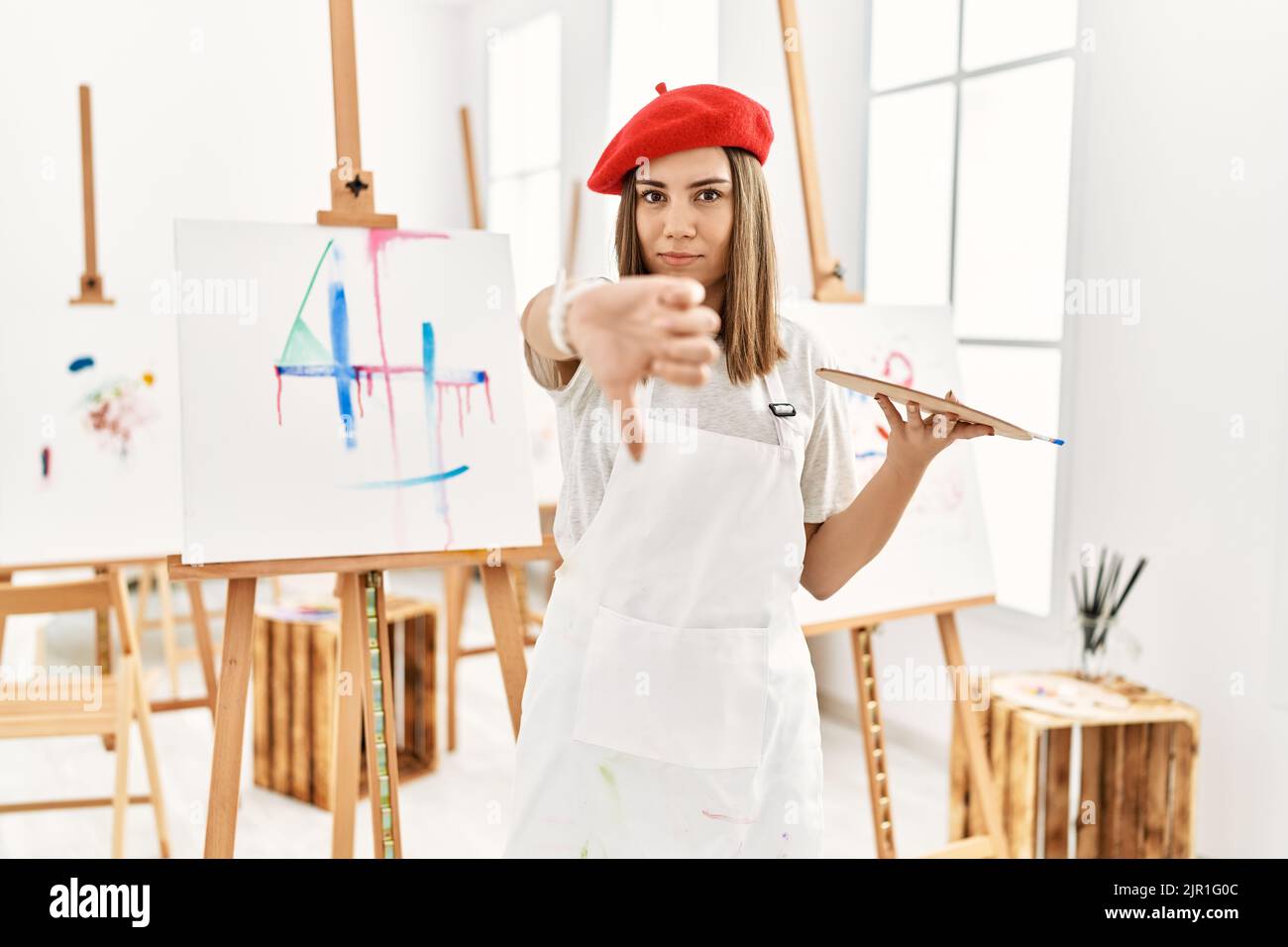Young artist woman painting on a canvas at art studio looking unhappy ...